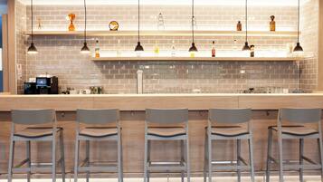 Uma área de bar moderna com painel de azulejos, iluminação pendente e banquetas.