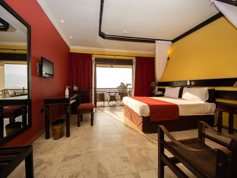 Quarto de hotel com cama, escrivaninha, cadeira e televisão.