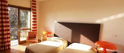 Quarto de hotel com duas camas, uma cadeira e uma varanda com cortinas.