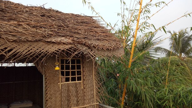 Uma cabana com telhado de palha, uma pequena janela e um abajur amarelo pendurado.