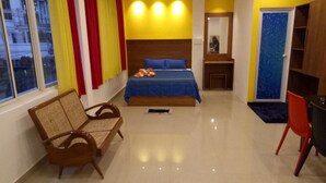 Quarto de hotel com cama, duas cadeiras de madeira, uma mesinha e um espelho.