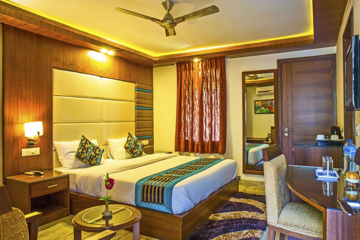 Quarto de hotel com uma cama grande, uma escrivaninha, uma cadeira, uma mesa redonda, um ventilador de teto e uma televisão.