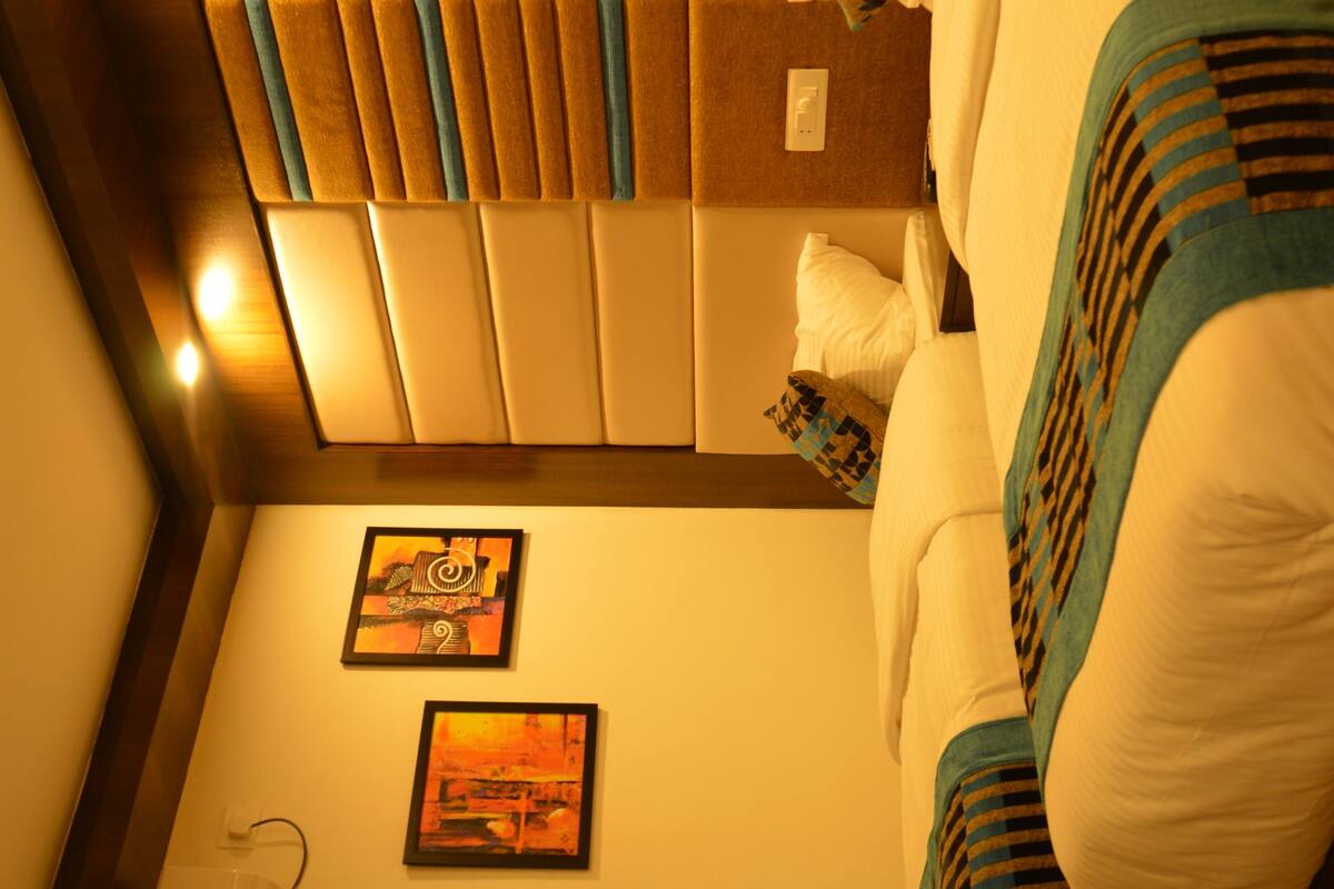 Quarto de hotel com uma cama, um aquecedor fixado na parede e duas fotografias emolduradas.