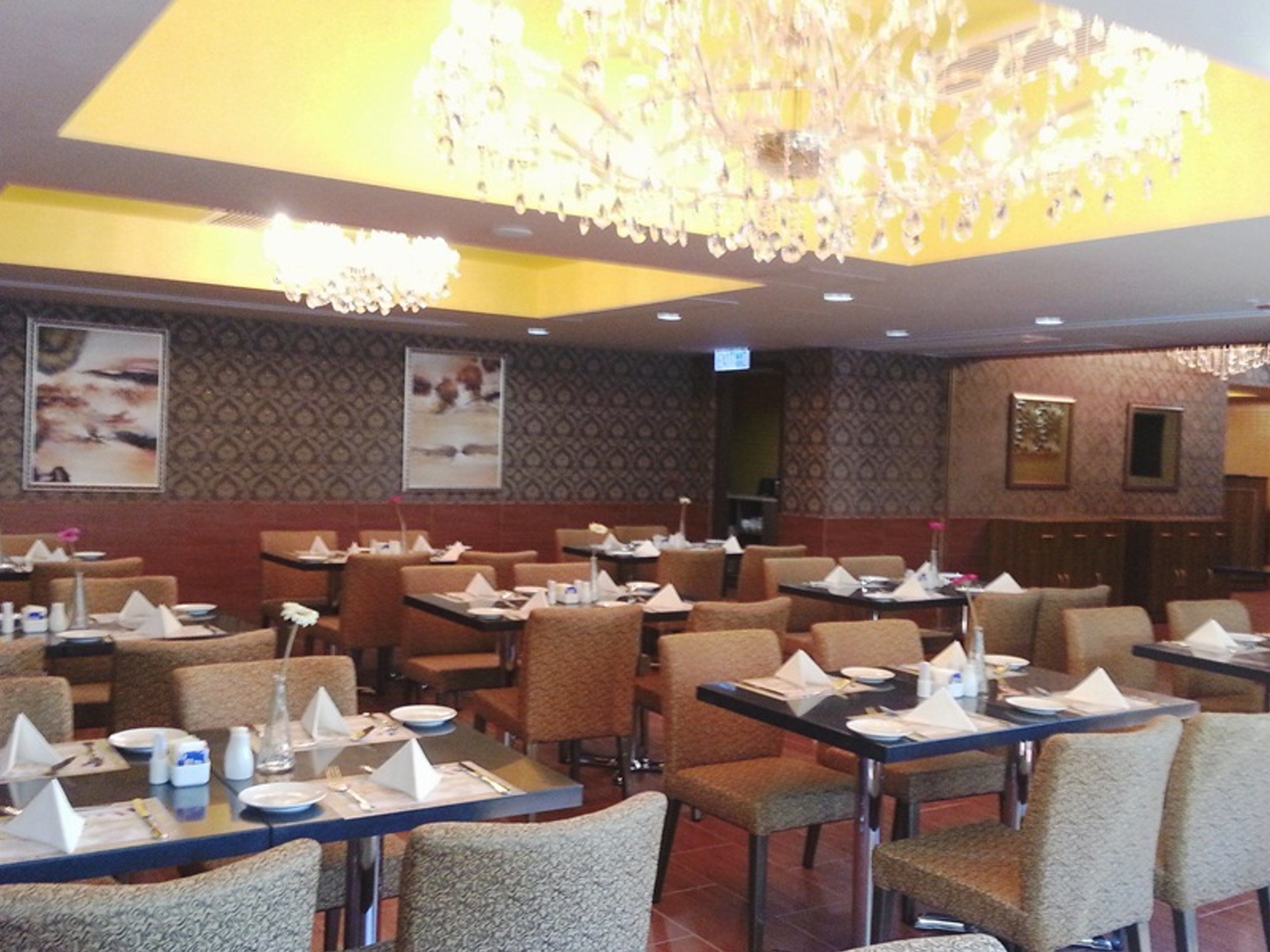 Uma sala de jantar com mesas preparadas para o serviço, um candelabro e papel de parede estampado.