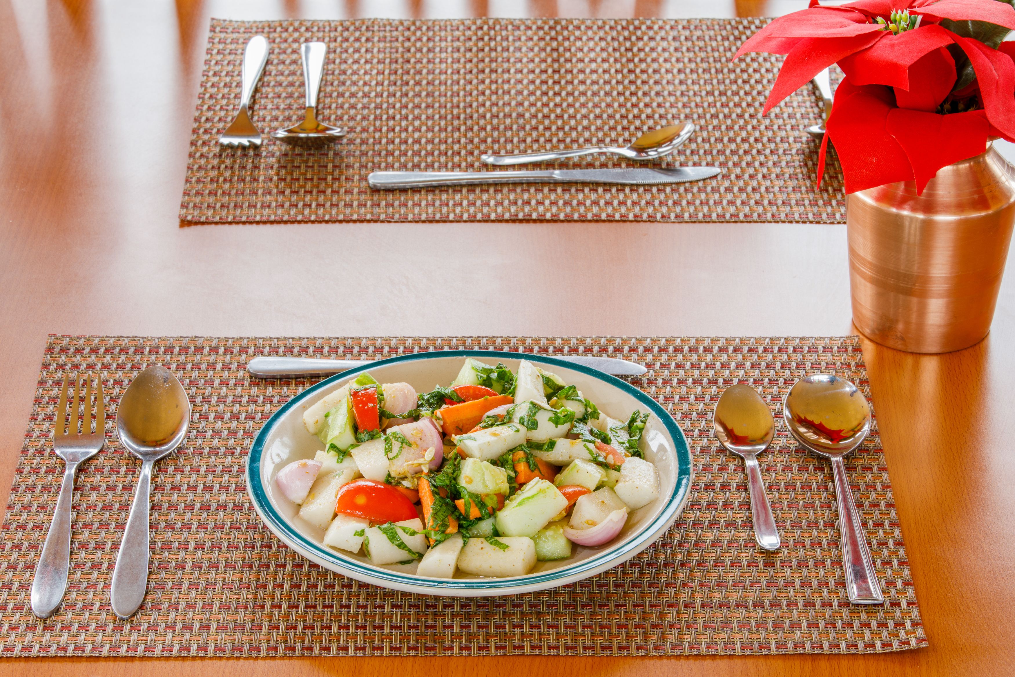Uma mesa posta com uma saladeira, talheres e um copo de cobre.