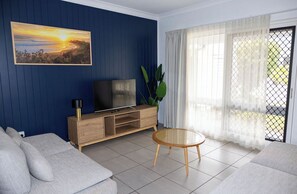 Uma sala de estar com televisão, sofá e uma mesa redonda.