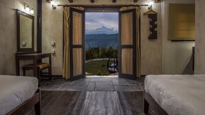 Quarto com duas camas, piso de madeira, vista para montanhas e uma cadeira suspensa no exterior.