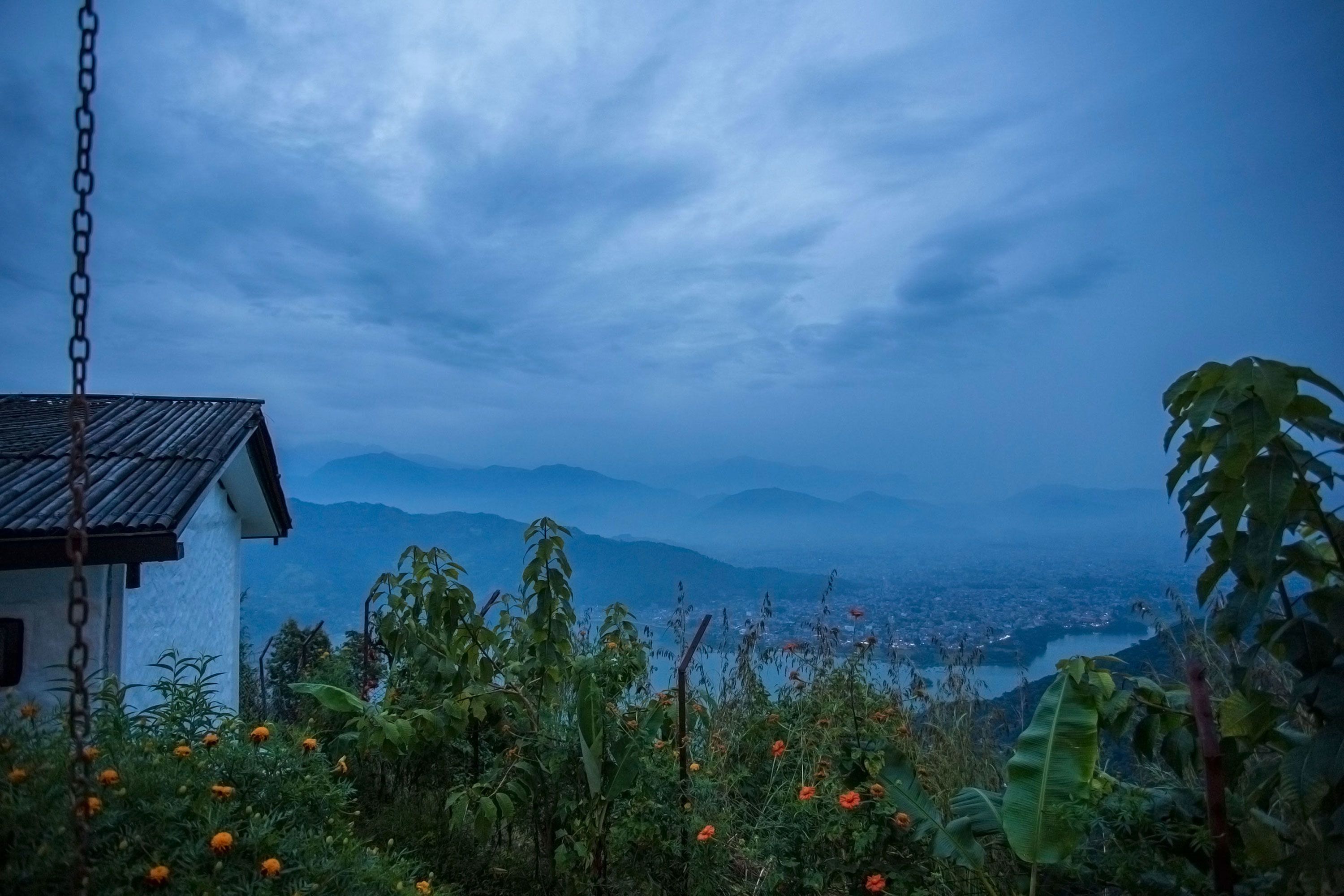 Vista de uma paisagem montanhosa com uma casa e um jardim em primeiro plano.