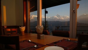 Mesa posta com talheres e pratos, com vista para montanhas cobertas de neve através de uma janela.