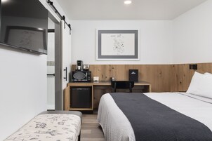 Quarto de hotel moderno com uma cama, uma escrivaninha com um computador, um micro-ondas e uma cafeteira.