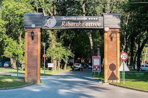 Um portão de entrada com uma placa indicando "Turističko naselje Ribarsko ostrvo" e uma placa de limite de velocidade de 20 km/h.