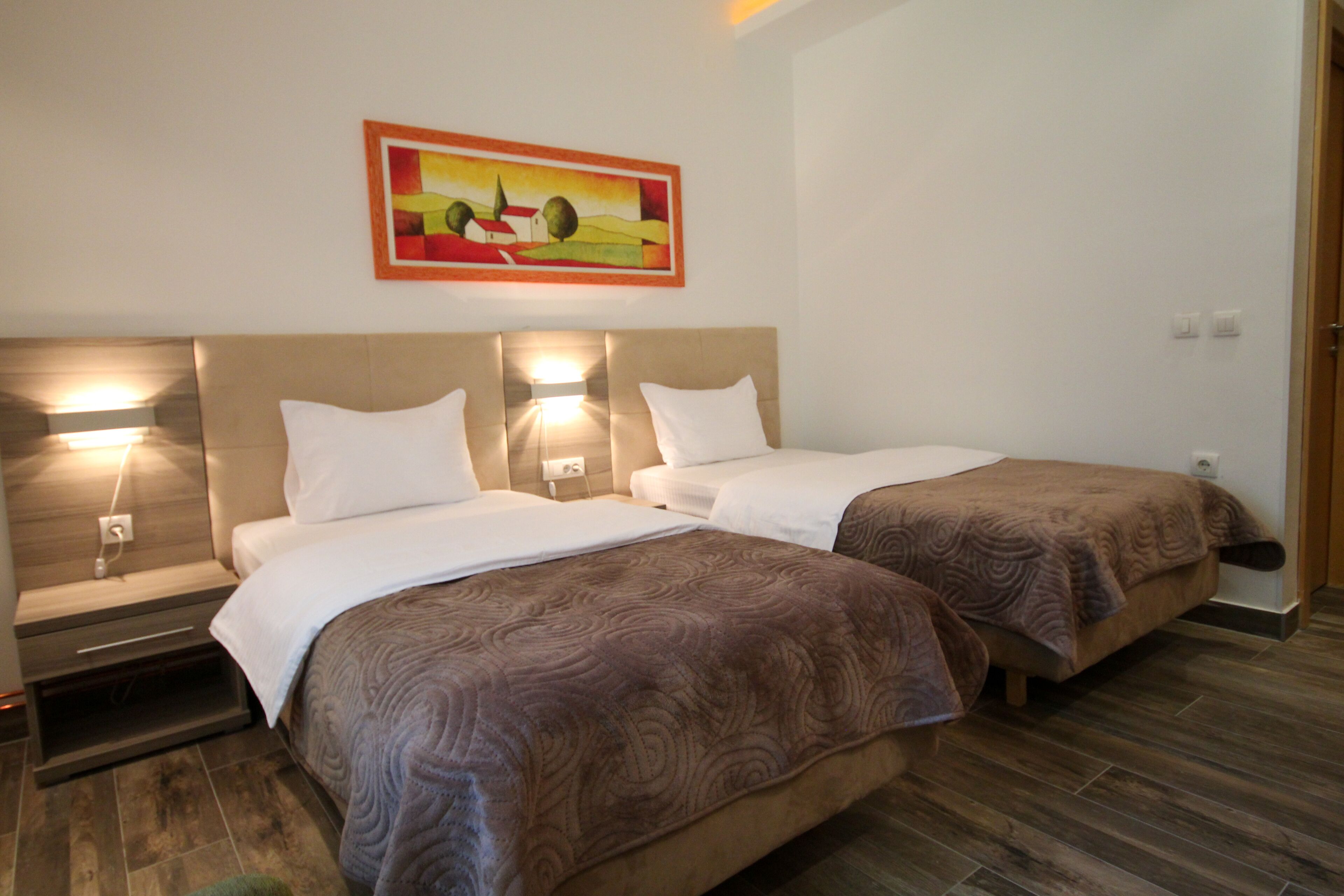 Quarto de hotel com duas camas, um quadro na parede e piso de madeira.
