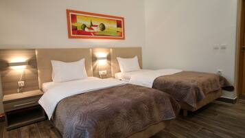 Quarto de hotel com duas camas, um quadro na parede e piso de madeira.