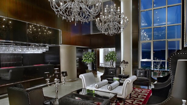 Uma sala de estar luxuosa com uma grande televisão de tela plana, elegantes lustres e uma ampla janela com vista para a cidade.