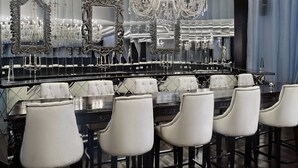 Uma sala de jantar luxuosa com uma mesa comprida, várias cadeiras, espelhos ornamentados e lustres.