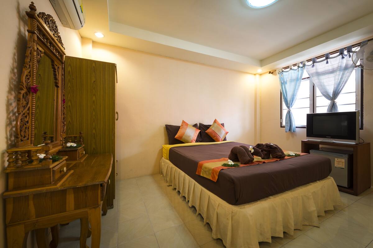Quarto de hotel com cama, televisão, penteadeira e espelho.
