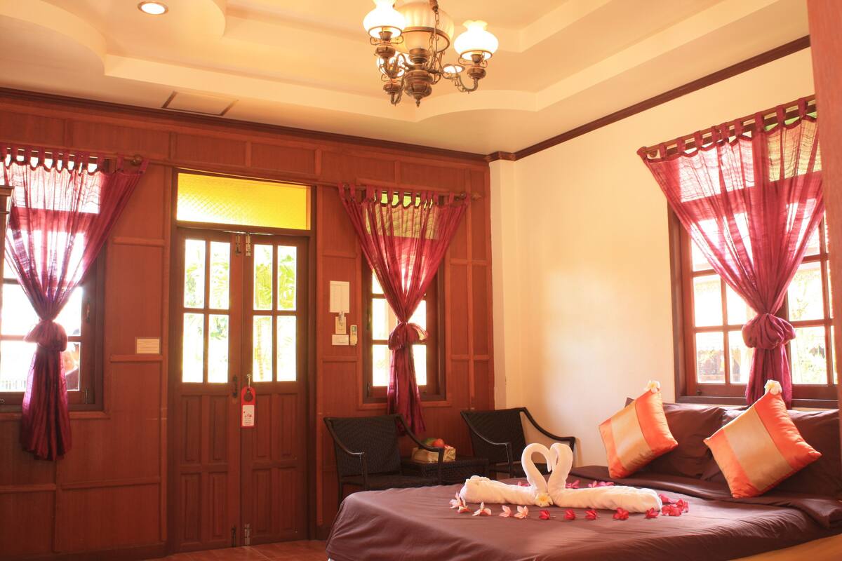 Quarto de hotel com painéis de madeira, uma cama com um buquê de flores, duas cadeiras e um candelabro.