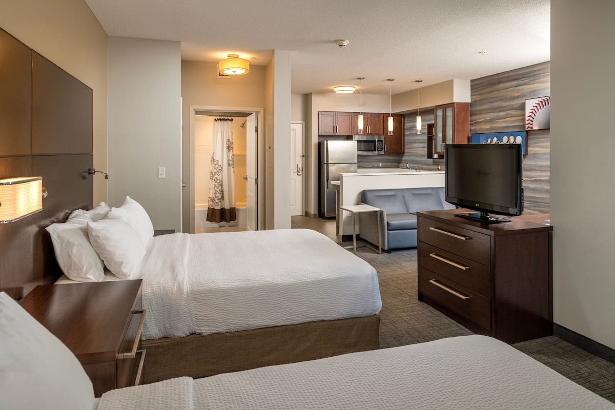Quarto de hotel com duas camas, televisão, secretária e cozinha compacta.