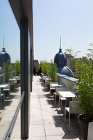 Terraço no telhado com área de estar ao ar livre, plantas em vasos e vista de edifícios com cúpulas ao fundo.