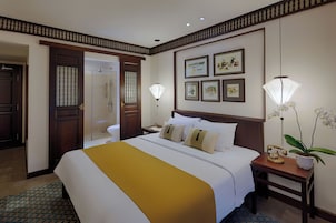 Quarto de hotel com uma cama grande, uma mesa de cabeceira com abajur, uma orquídea em vaso e quadros nas paredes.