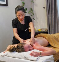 Sessão de massagem em um quarto com cama, maciez de massagem, uma planta e uma mesinha com uma garrafa e uma tigela.