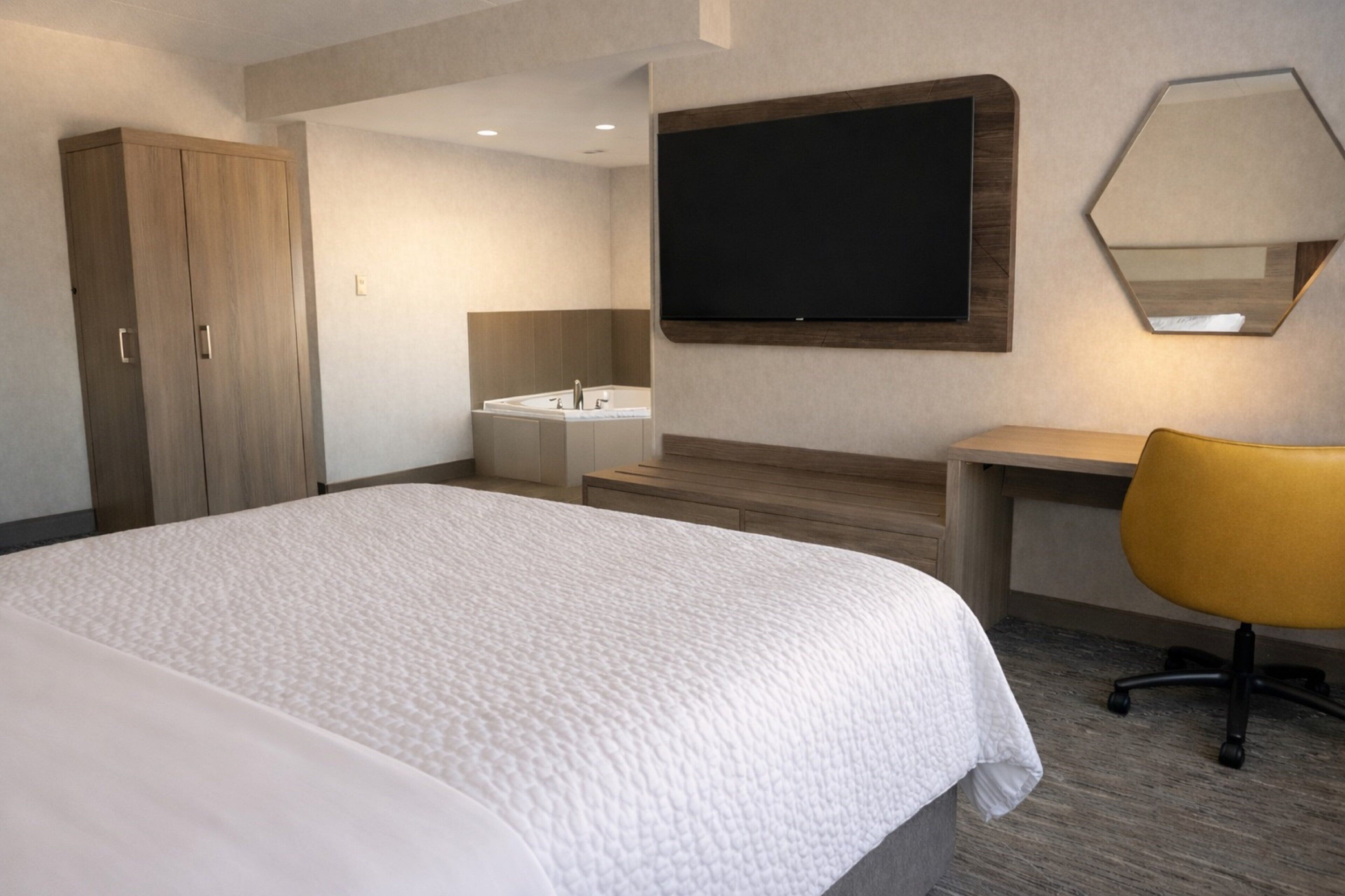 Quarto de hotel com uma cama grande, uma escrivaninha, uma cadeira, uma televisão e um banheiro com banheira.