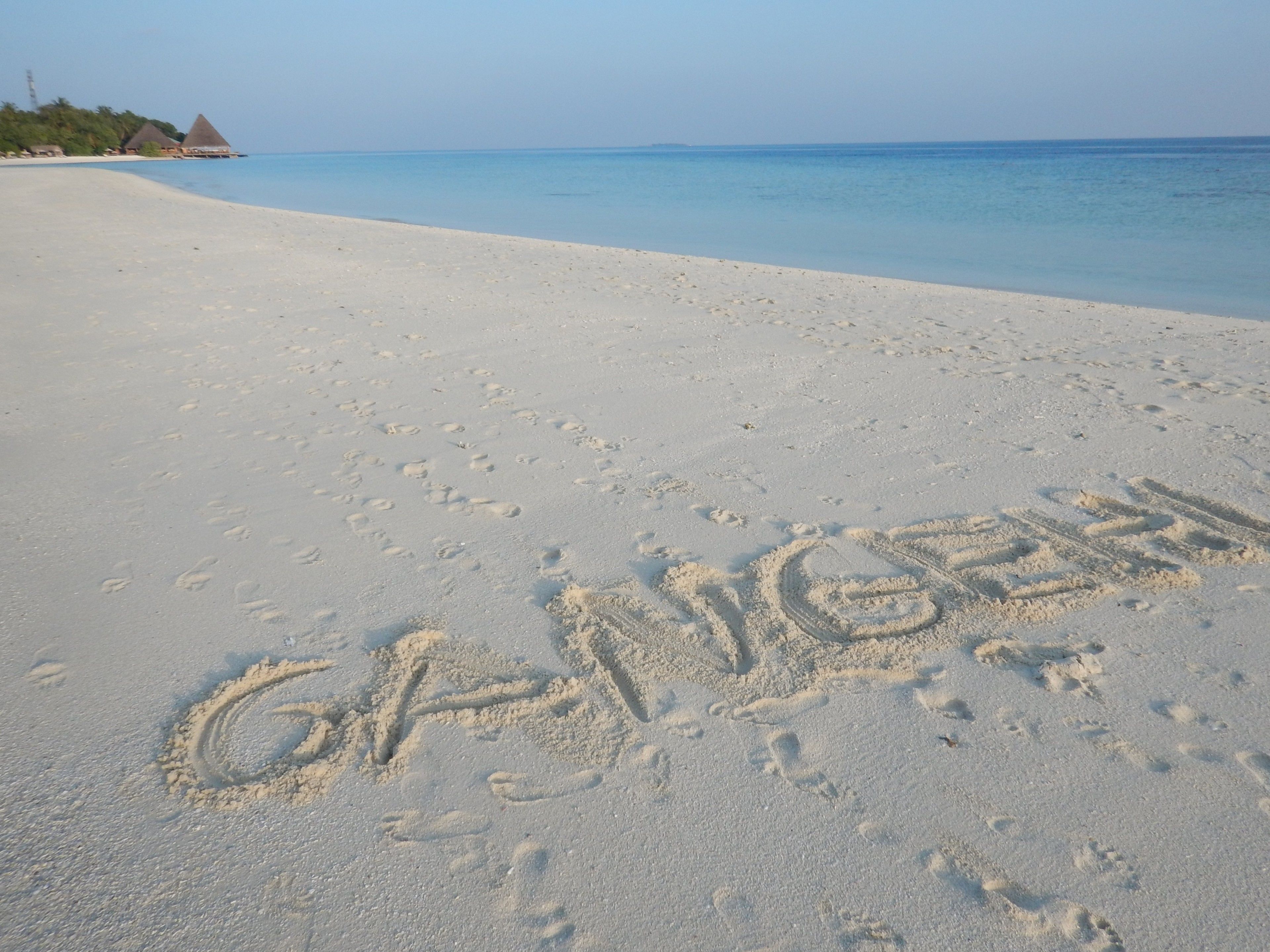 Uma praia com pegadas e a palavra 'CANDENI' escrita na areia.