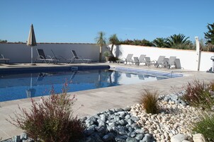 Piscina com espreguiçadeiras e um pequeno guarda-sol, rodeada por pedras e plantas.