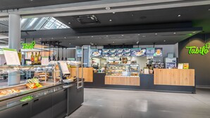 Uma área moderna de alimentação, com uma vitrine de vidro, balcões de madeira e um quadro de cardápio.