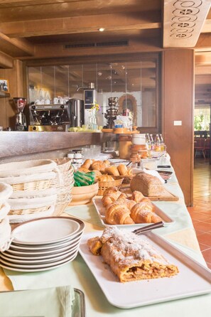 Buffet com diversos pães, doces e uma máquina de café.