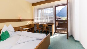 Quarto de hotel com uma cama, uma mesa de trabalho e vista para montanhas através de uma janela grande.