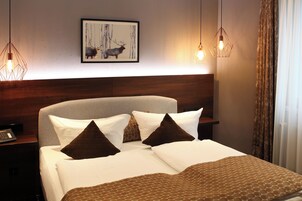 Cama bem arrumada com colcha estampada, quadro com imagem de alce na parede e duas luminárias pendentes.