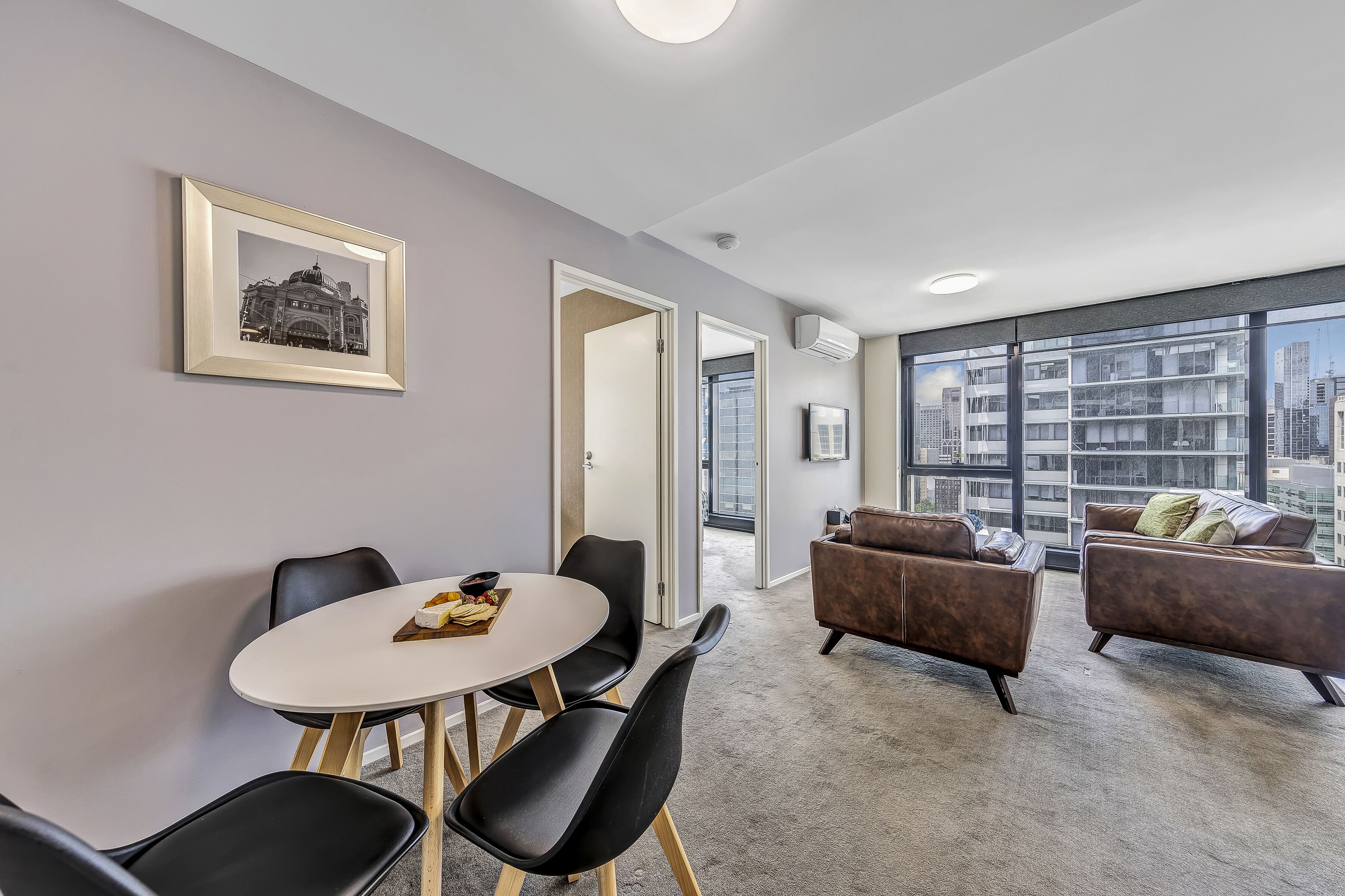 Uma sala de estar moderna com área de jantar, janelas amplas com vista para a cidade e um quadro na parede.