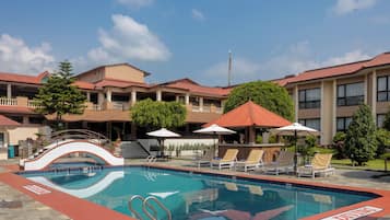 Piscina com espreguiçadeiras e guarda-sóis, cercada por edifícios com telhados vermelhos e céu claro.