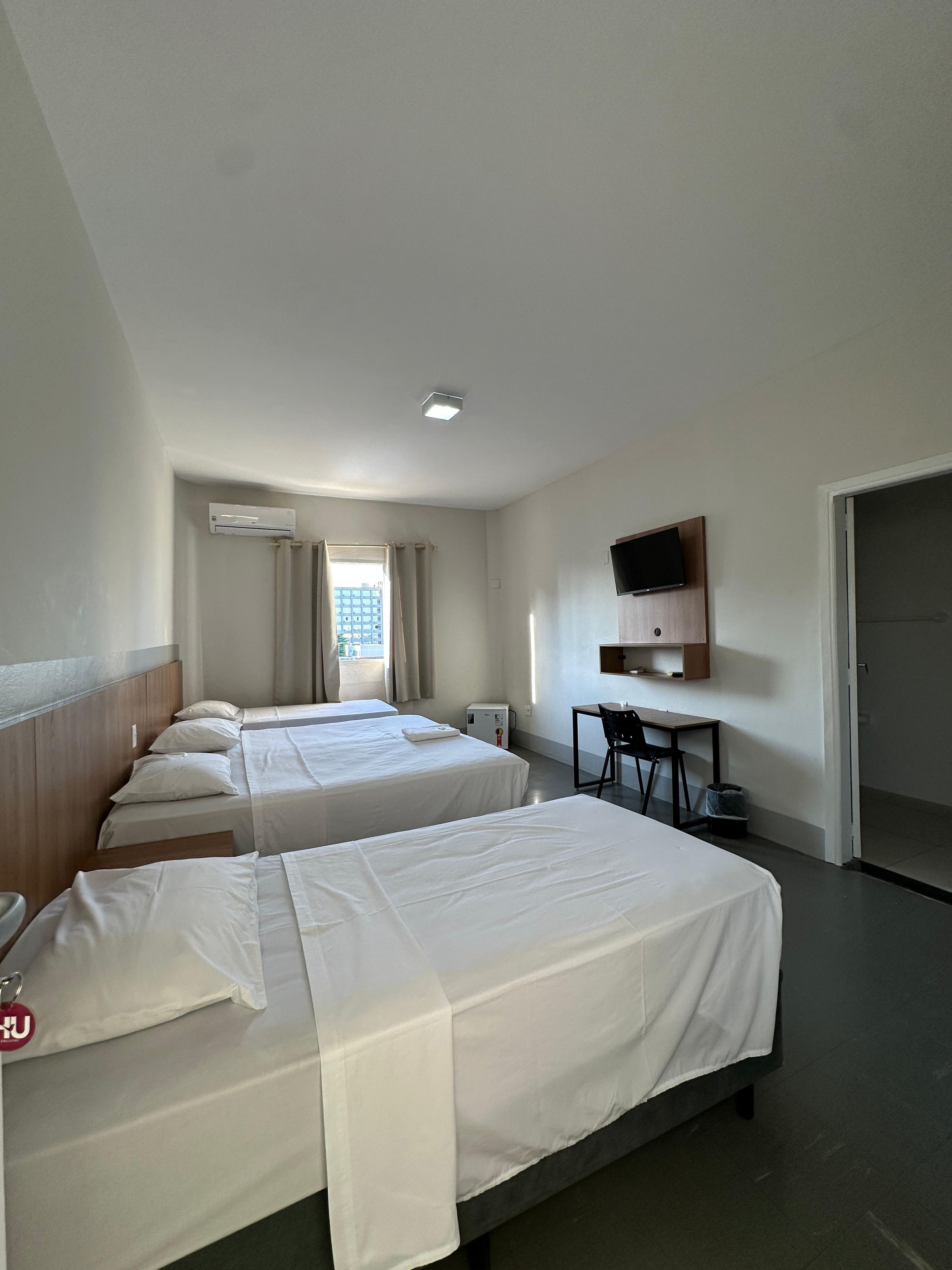 Quarto de hotel com duas camas, uma escrivaninha, uma cadeira, uma televisão e um ar condicionado.