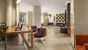 Um lobby moderno com balcão de recepção de madeira, assentos em tons de roxo e laranja, e um balcão de check-in.