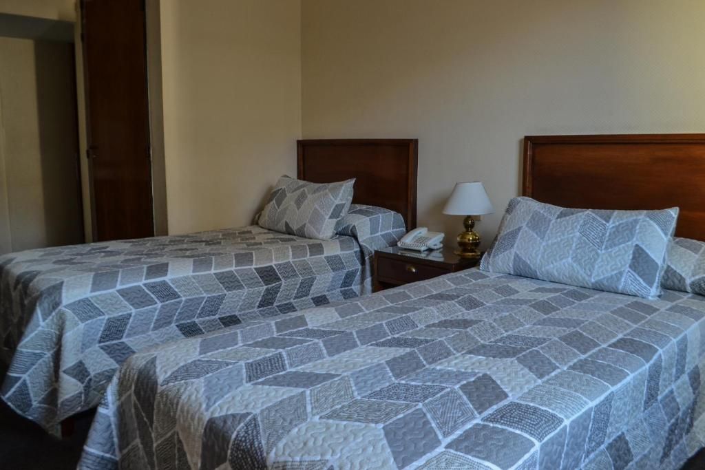 Quarto de hotel com duas camas, cada uma com colcha estampada, mesa de cabeceira com abajur e telefone.