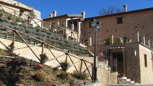 Um edifício de pedra com escadaria que leva a uma varanda, rodeado por vegetação.