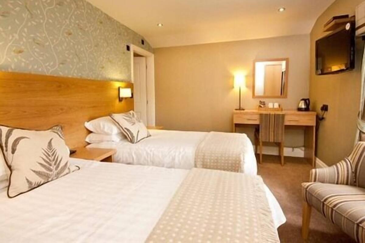 Quarto de hotel com duas camas, uma escrivaninha, uma cadeira e um espelho.