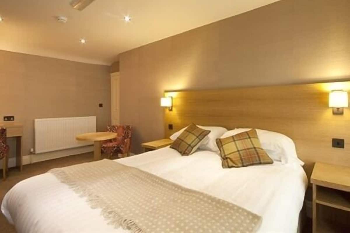 Quarto de hotel com uma cama grande, duas mesas de cabeceira, uma cadeira e um radiador.