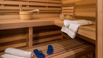 Um banco de sauna de madeira com uma toalha e chinelos, um balde de madeira e duas taças de água.