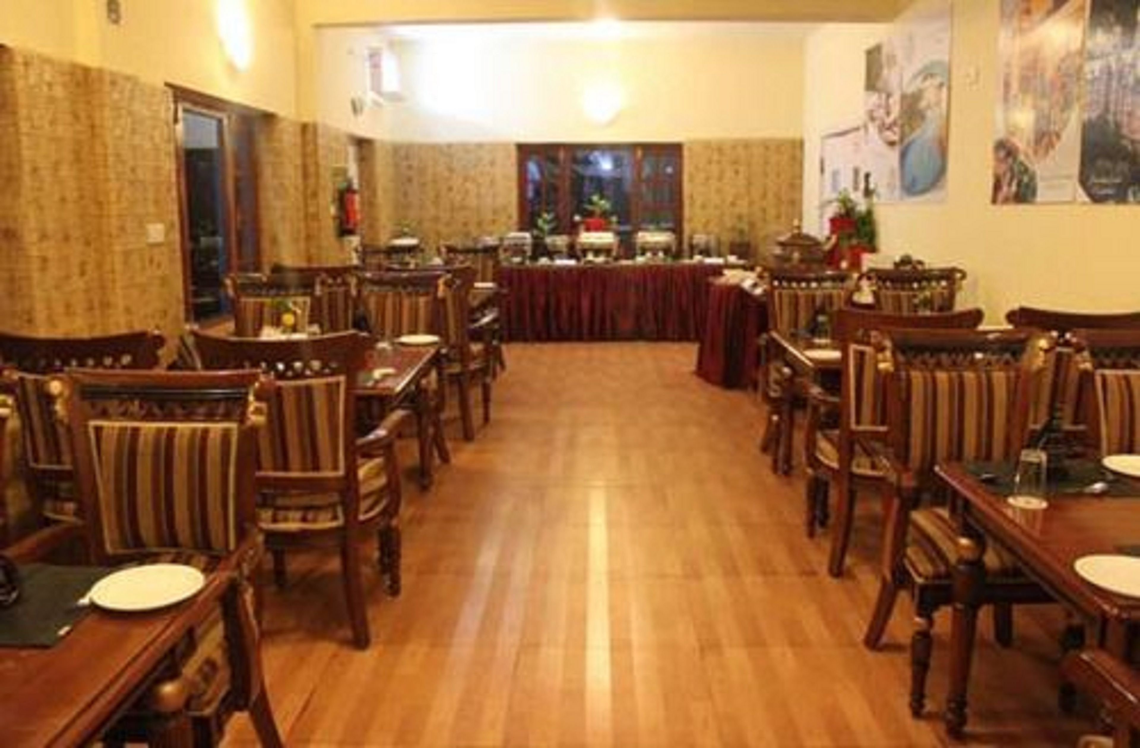 Uma sala de jantar com mesas e cadeiras de madeira, uma mesa de buffet central e uma parede estampada.
