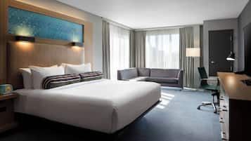 Quarto de hotel com uma cama grande, uma escrivaninha, uma cadeira e televisão na parede.