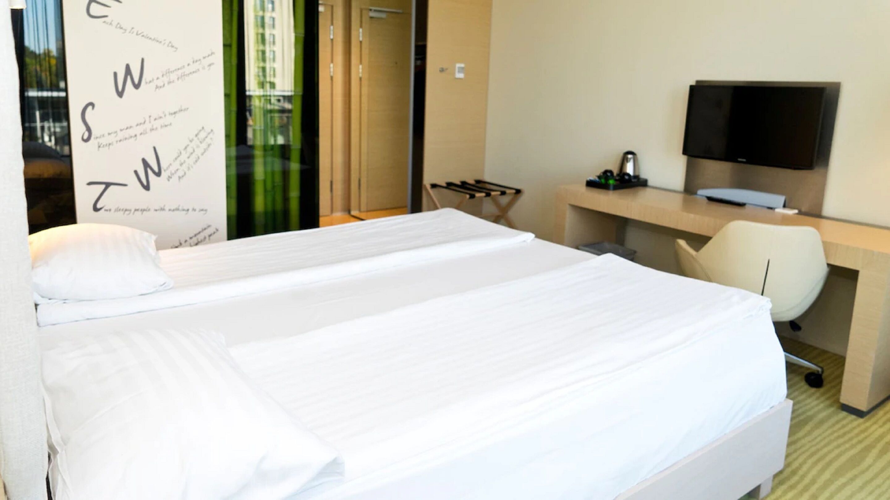 Quarto de hotel com cama, escrivaninha e televisão, e uma cadeira.