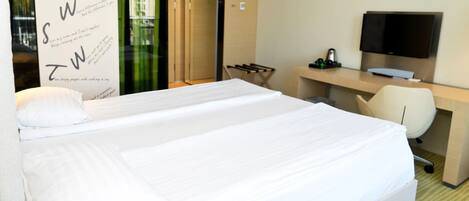 Quarto de hotel com cama, escrivaninha e televisão, e uma cadeira.