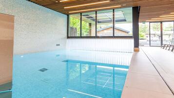 Piscina interna com água cristalina, teto de madeira e grandes janelas.
