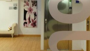 Uma área de recepção com um sofá, um grande quadro floral e um elevador moderno.