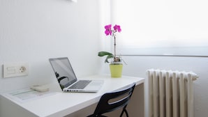 Uma mesa branca com um laptop, uma orquídea em vaso e um radiador.