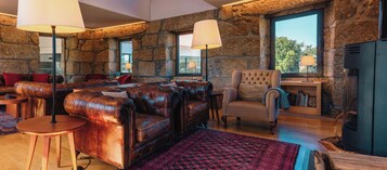 Uma sala de estar acolhedora com um sofá de couro, poltronas e uma televisão. O espaço apresenta paredes de pedra e janelas amplas.