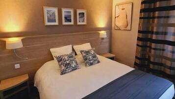 Quarto de hotel com cama, abajures, cabeceira, mesa de cabeceira, um quadro na parede e uma janela com cortina.